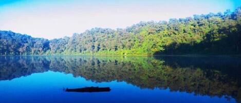 Um lago tranquilo com um barco em primeiro plano e colinas florestadas ao fundo.