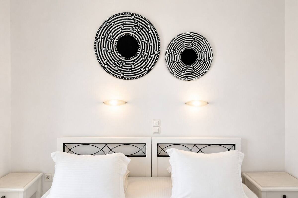 Uma cama de casal com roupa de cama branca, duas mesas de cabeceira e luminárias circulares fixadas na parede.