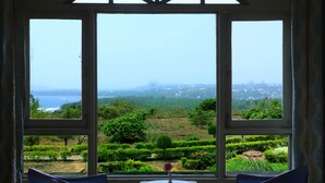 Quarto com uma janela ampla que oferece vista para um jardim ajardinado e um horizonte urbano distante.
