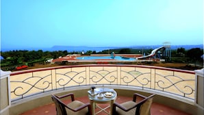 Uma varanda com mesa e cadeiras, com vista para uma piscina e uma paisagem panorâmica do oceano e das colinas.