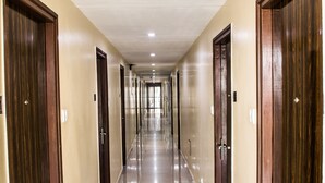 Um corredor longo e bem iluminado, com portas de madeira em ambos os lados e um chão de azulejos brilhante.