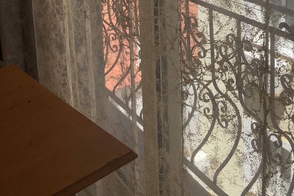 Vista pela janela, com grade de metal, varanda e um prédio ao fundo.