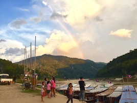 Margem de rio com barcos, um arco-íris e uma paisagem montanhosa.