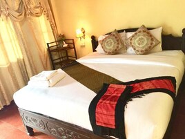 Uma cama bem arrumada com manta vermelha e preta, dois travesseiros e uma mesa de cabeceira com abajur.