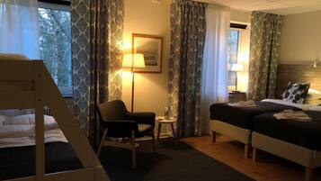 Quarto de hotel com duas camas, uma cadeira, uma mesa pequena e um abajur.