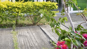 Uma casa com persianas verdes, varanda branca e um pequeno jardim com flores amarelas e cor-de-rosa.
