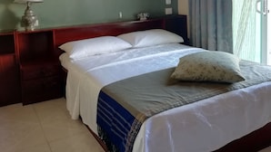 Quarto de hotel com cama, mesa de cabeceira, luminária, quadro na parede e janela com cortinas.