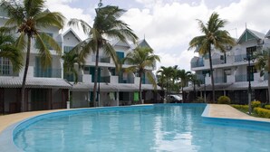 Piscina rodeada por edifícios altos com varandas, palmeiras e céu claro.