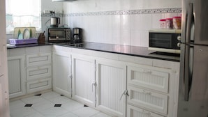 Cozinha com armários brancos, bancada preta e geladeira de aço inoxidável.