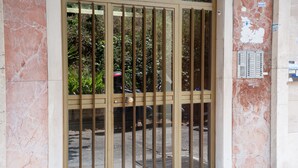 Uma entrada murada com portão de metal e uma pequena abertura na parede.