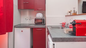 Cozinha compacta com torradeira, pequeno frigorífico e máquina de café.
