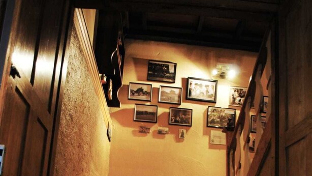 Uma escadaria de madeira com corrimão, que leva a um patamar com uma parede decorada com fotografias emolduradas.