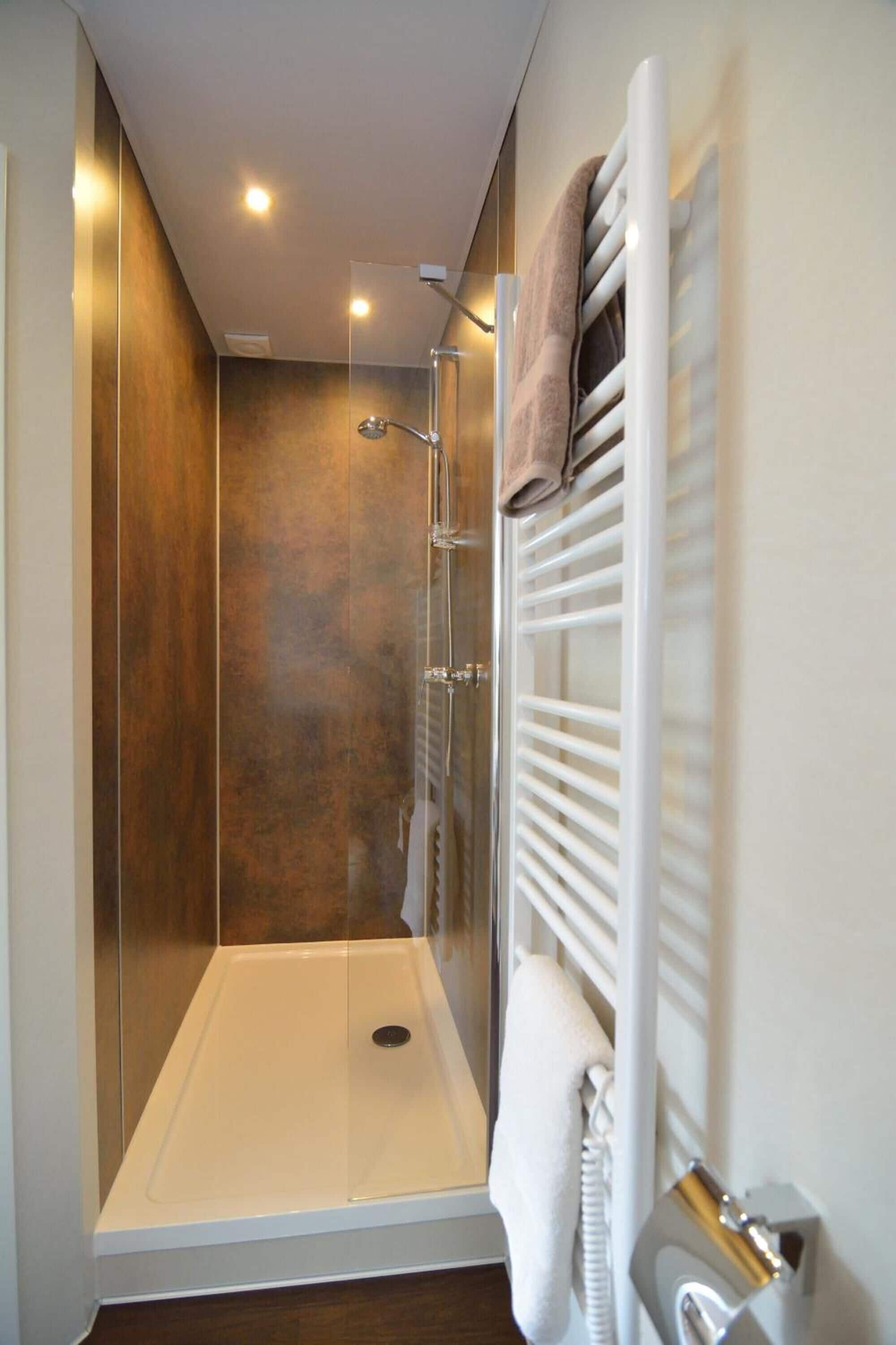 Um banheiro moderno com chuveiro em box de vidro, porta-toalhas branco e aquecedor embutido.