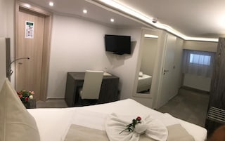 Quarto de hotel com cama, escrivaninha, cadeira, televisão e banheiro.