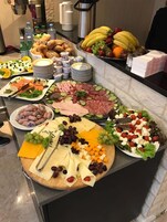 Buffet com diversas opções de alimentos, incluindo frutas, queijos, carnes e saladas.