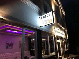 Exterior de hotel com a placa 'HOTEL Sophia', um restaurante 'Ristorante da Panto' e um pinheiro de Natal visível pela janela.
