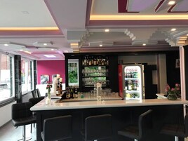 Uma área de bar com balcão, banquetas, prateleiras com garrafas e copos, e um refrigerador Coca-Cola.