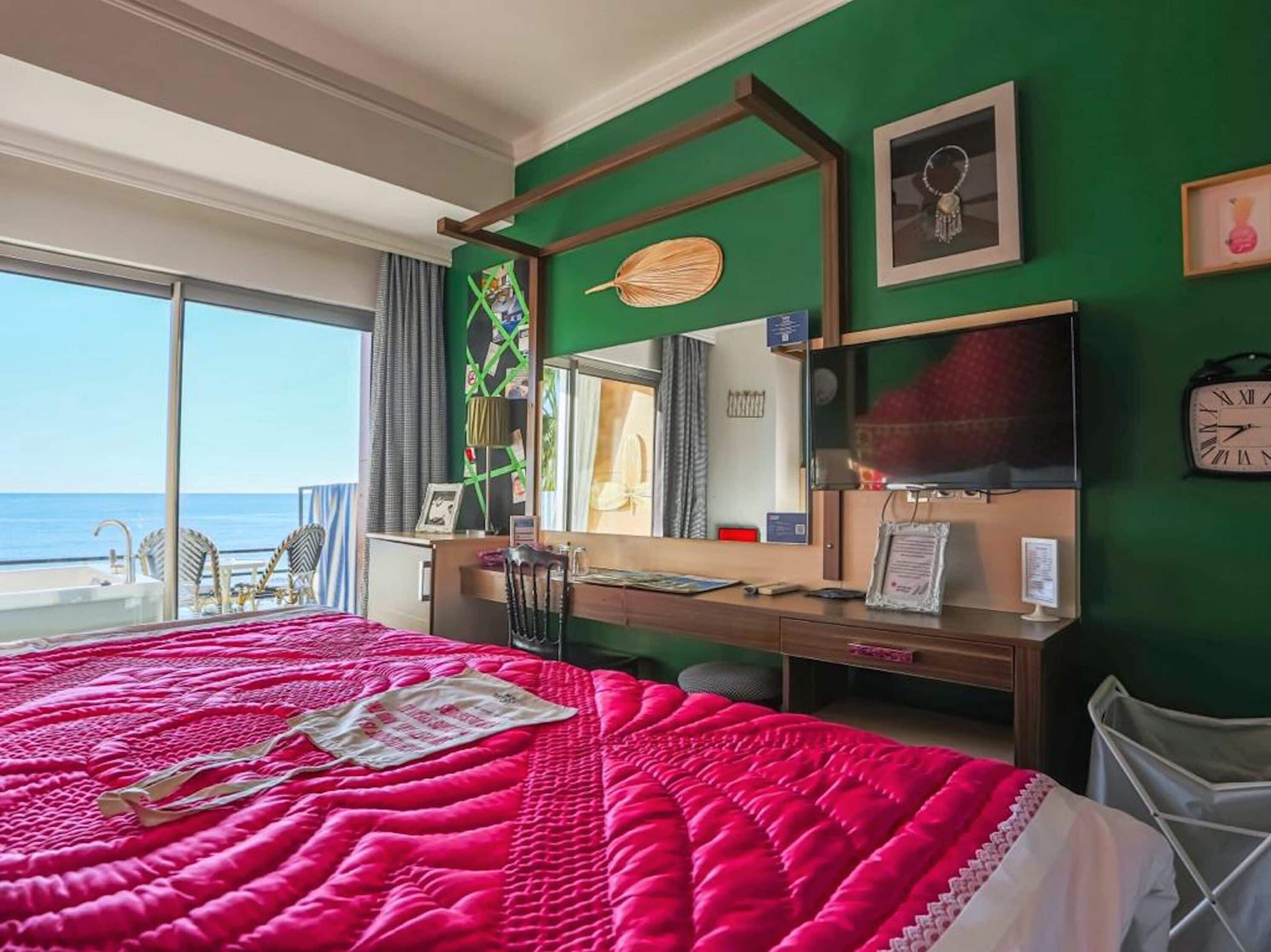 Quarto de hotel com uma cama grande, uma escrivaninha, uma cadeira, uma televisão e vista para o oceano.