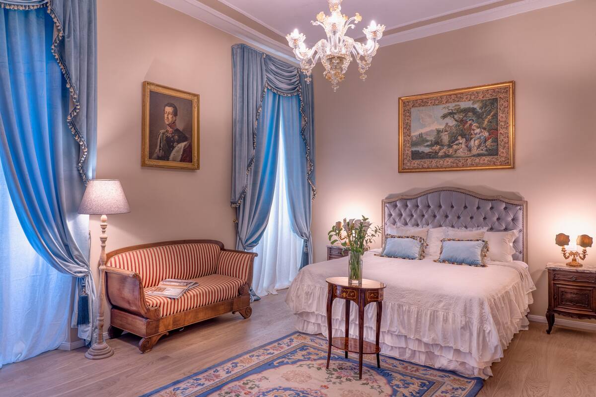 Um quarto com uma cama grande, uma cadeira de madeira, uma mesa de cabeceira com abajur e um quadro na parede.