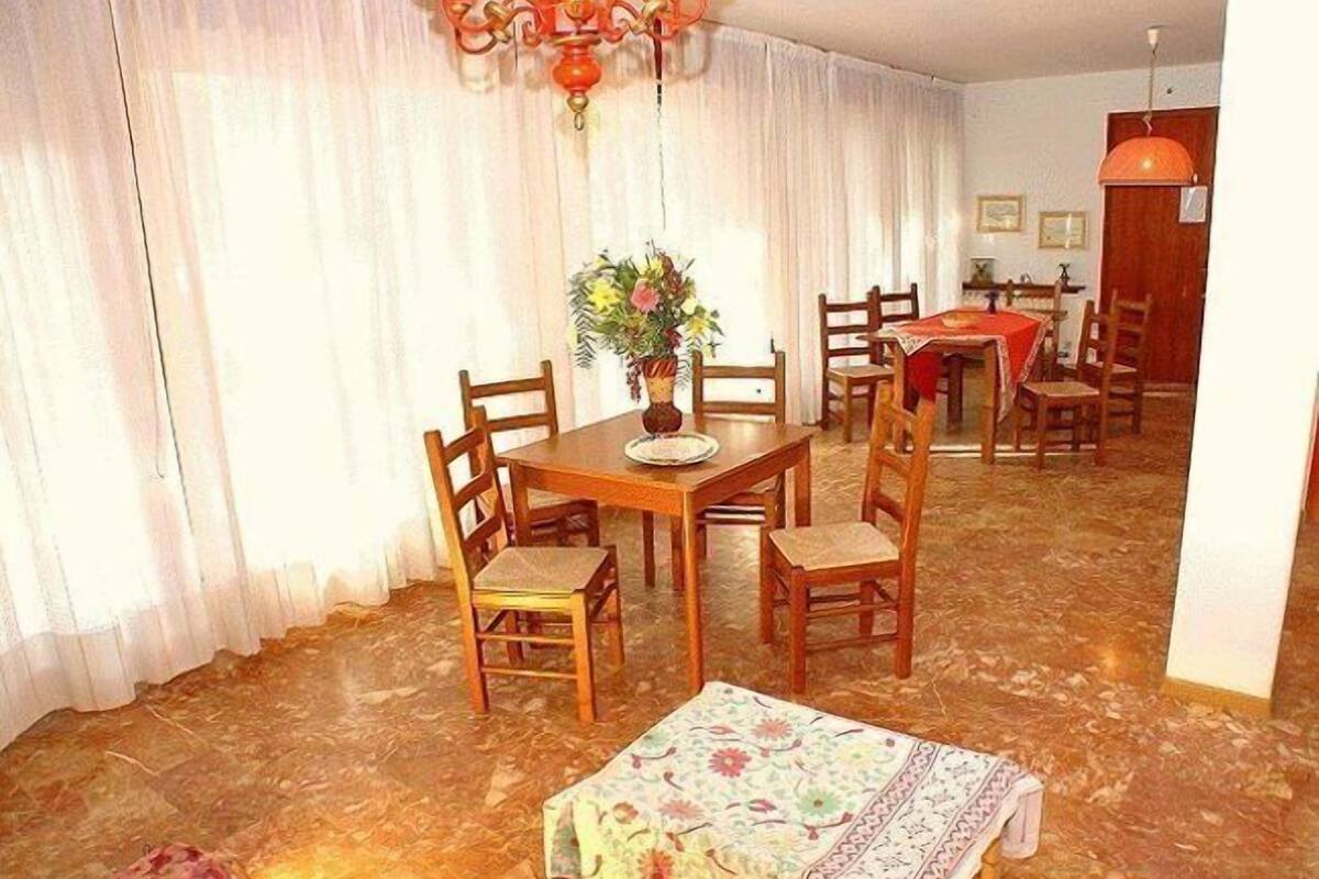 Uma área de refeições com mesa de madeira, cadeiras, um vaso com flores e um jogo de mesa estampado.