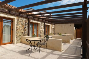 Um pátio ao ar livre com paredes de pedra, pérgola de madeira e áreas de estar.
