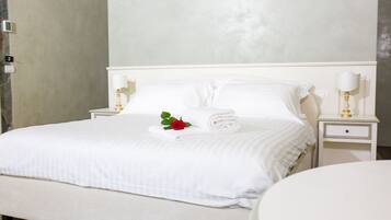 Cama bem arrumada com lençóis brancos, uma rosa vermelha e duas luminárias de cabeceira.