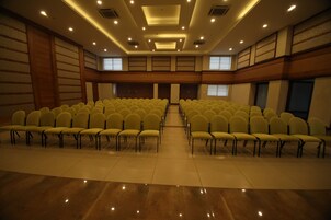 Uma sala de conferência com fileiras de cadeiras amarelas, piso de mármore polido e teto alto com iluminação embutida.