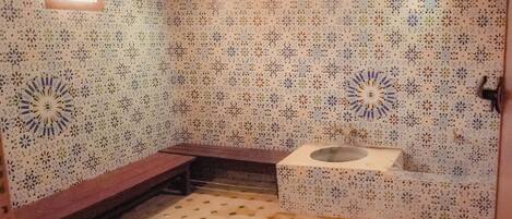 Quarto com paredes estampadas, um banco, uma pia e piso ladrilhado.