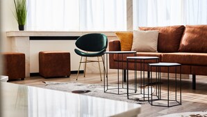 Uma sala de estar moderna com um sofá marrom, uma poltrona verde e mesas laterais de metal preto.