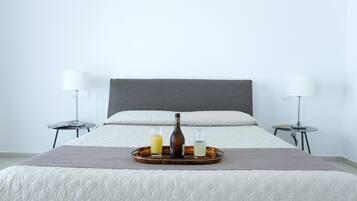 Cama bem arrumada com uma bandeja de bebidas e uma garrafa, duas luminárias de cabeceira e uma parede lisa.