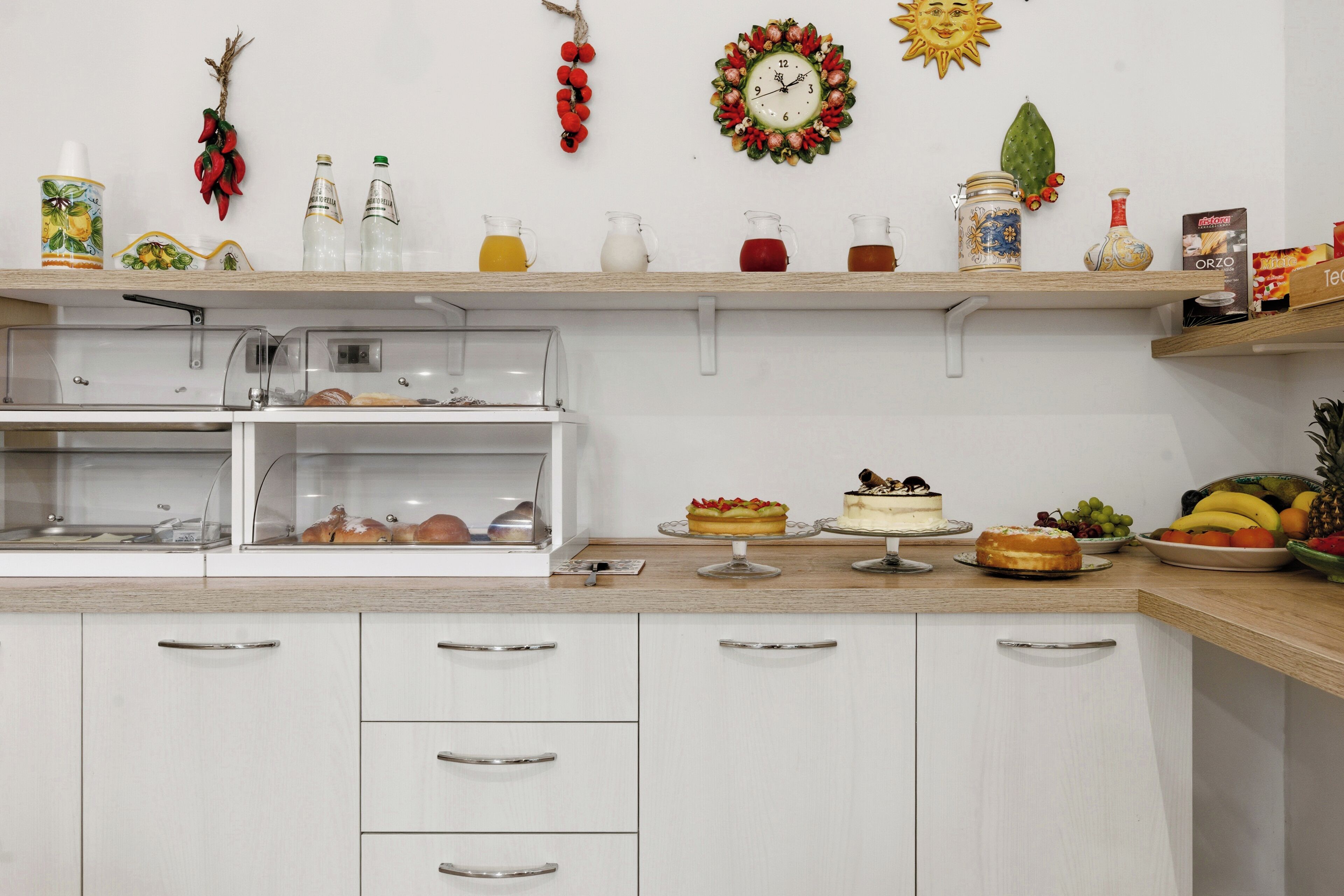 Cozinha com armários brancos, bancada de madeira e diversos alimentos e objetos decorativos.