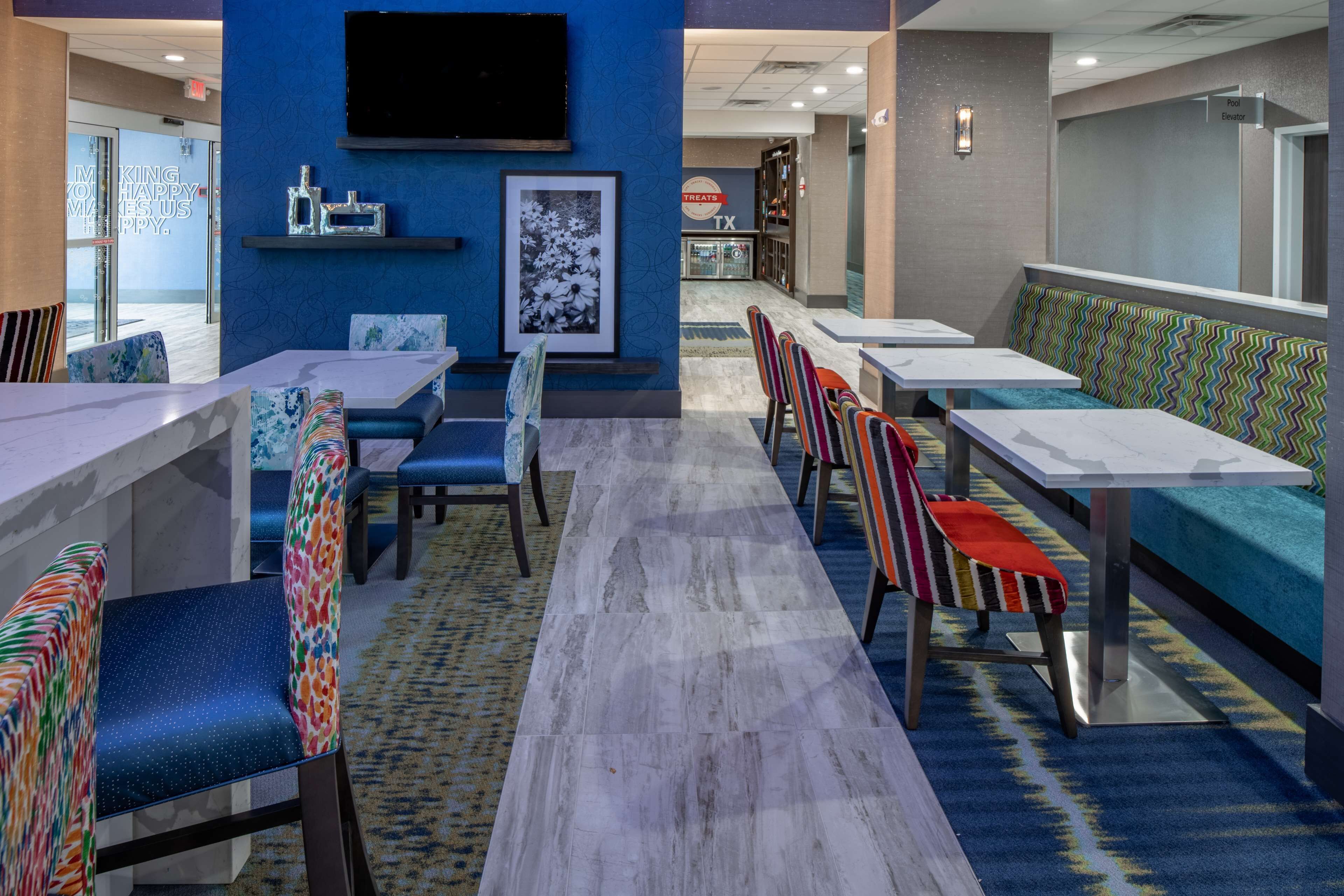 Um restaurante com um balcão comprido, cadeiras coloridas e um tapete azul.