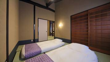 Quarto de hotel com duas camas, uma porta deslizante de madeira e uma pequena luminária fixada na parede.