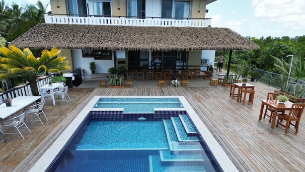 Uma área de piscina com deck de madeira, assentos e um edifício com telhado de palha.