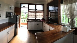 Uma cozinha com armários brancos, micro-ondas, geladeira e pia. Há uma janela com cortinas e vista para o verde lá fora.
