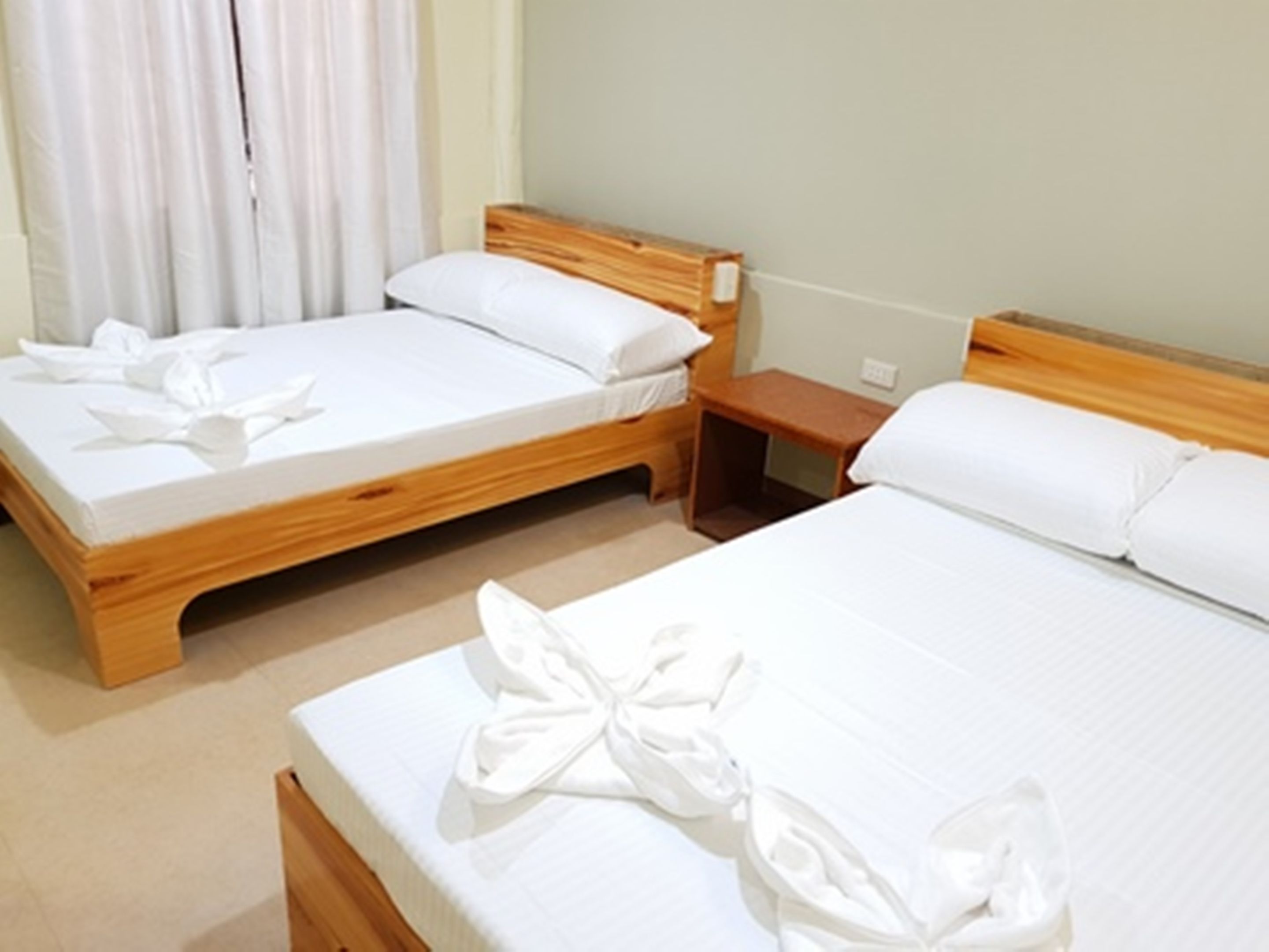Quarto de hotel com duas camas de madeira, roupa de cama branca e uma pequena mesa de cabeceira de madeira.