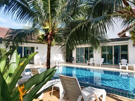 Piscina com espreguiçadeiras, uma palmeira e um edifício com grandes janelas.