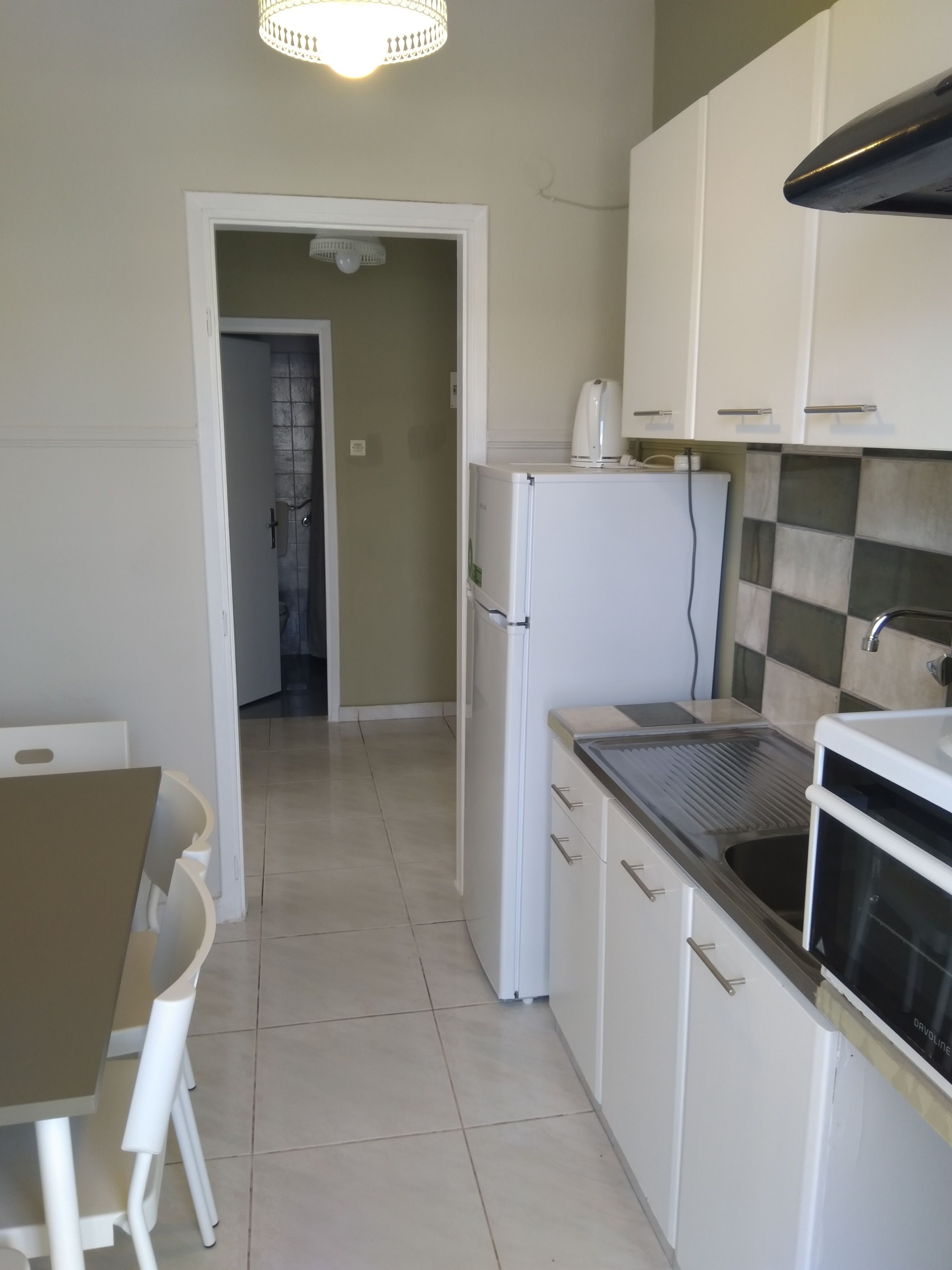 Uma cozinha compacta com armários brancos, forno embutido e uma pia.