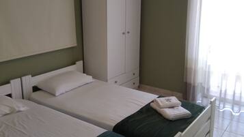 Quarto de hotel com duas camas, um guarda-roupa, um candeeiro e uma janela com cortinas.