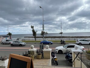 Uma estrada costeira com carros e motocicletas estacionados, um poste de luz e vista para o oceano.