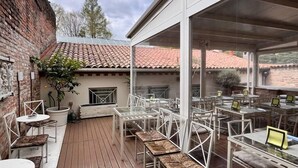 Um pátio externo com piso de madeira, cadeiras e mesas de metal branco, algumas com laptops.