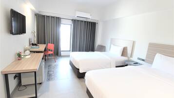 Quarto de hotel com duas camas, uma escrivaninha com cadeira, televisão e ar condicionado.