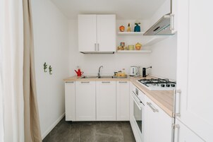 Uma cozinha compacta com armários brancos, fogão, pia e bancada pequena.
