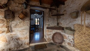 Interior rústico em pedra com teto de madeira, paredes de pedra, área de refeições e diversos utensílios de cozinha.