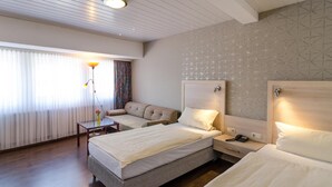 Quarto de hotel com cama grande, sofá, mesa de cabeceira e luminária.