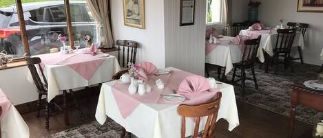 Uma área de refeições com mesas preparadas para o serviço, com um tapete estampado e cadeiras de madeira.