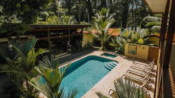 Piscina rodeada por vegetação exuberante, com espreguiçadeiras e área coberta.