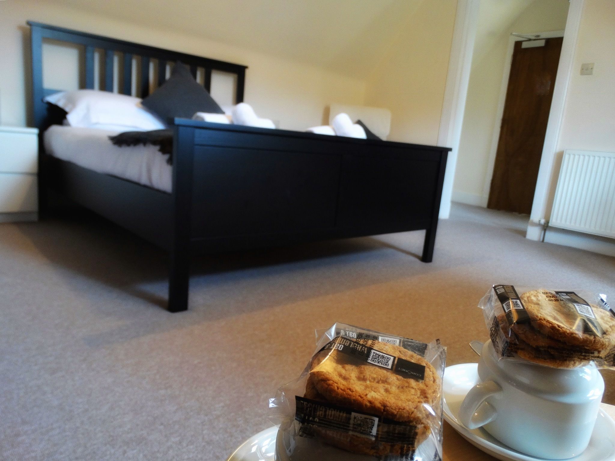 Quarto com uma cama, uma mesinha de cabeceira e um espaço para café da manhã com dois sanduíches embalados.