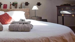 Cama bem arrumada com duas toalhas enroladas, um travesseiro vermelho e uma parede de tijolos decorada.