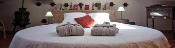 Cama bem arrumada com duas toalhas enroladas, um travesseiro vermelho e uma parede de tijolos decorada.